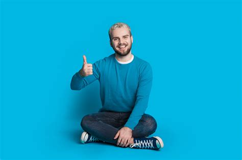 금발 머리를 가진 백인 남자의 흑백 사진은 파란색 벽에 포즈를 취하는 스튜디오에서 바닥에 앉아 T 셔츠에 대한 스톡 사진 및