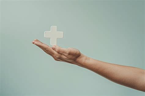Premium Photo Hand Presenting A White Cross Symbol On Pastel Background