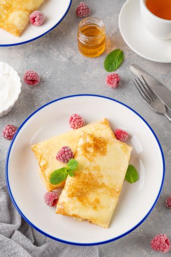 전통적인 얇은 팬케이크 또는 코티지 치즈 꿀 사워 크림 및 회색 콘크리트 배경에 차 한 잔과 함께 라스베리가있는 크레페 Maslenitsa를위한 음식 공간 복사 0명에 대한