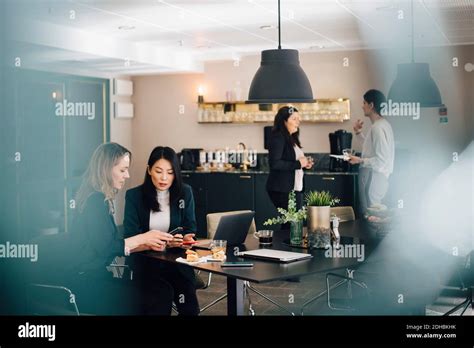 Businesswomen Using Smart Phones At Conference Table While Colleagues