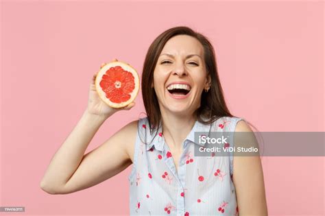 여름 옷에 젊은 여자를 웃 고 스튜디오에서 분홍색 파스텔 벽 배경에 고립 된 신선한 잘 익은 자 몽의 절반을 손에 잡고 사람들은 생생한 라이프 스타일 휴식 휴가 개념입니다