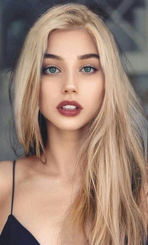 A Woman With Long Blonde Hair And Green Eyes Is Looking At The Camera While Wearing A Black Top