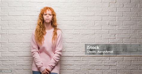 재미 있은 얼굴 뺨 피 벽돌 벽을 통해 서 젊은 빨강 머리 여자 입 어 미친 식으로 팽창 한 명의 여자만에 대한 스톡 사진 및