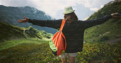 모자와 배낭을 메고 아름다운 산 초원 사이에 서 있는 손을 뻗은 젊은 여자 사진 Unsplash의 성공한 여성 이미지
