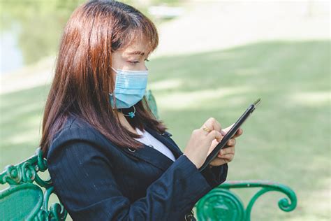 스마트 폰 태블릿을 사용하여 얼굴 마스크를 착용 하는 비즈니스 여성 일출 및 흐림 자연 배경 공원에서 응용 프로그램 장치와 함께
