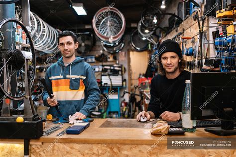 Positive Young Male Technician Assembling Bike While Colleague Working
