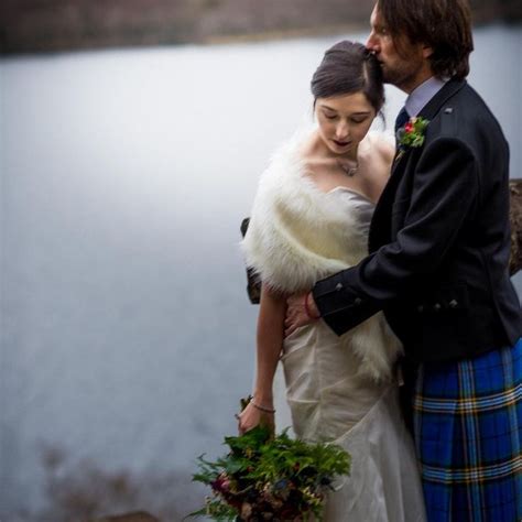 A Man And Woman Standing Next To Each Other In Front Of A Body Of Water