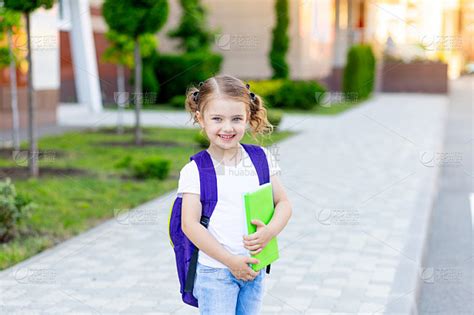 回到学校，一个女生背着书包，手里拿着一本书去上小学一年级
