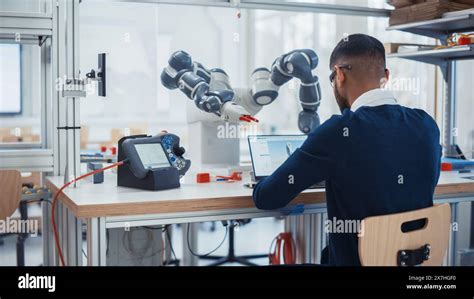 Male Industrial Robotics Engineer Uses Laptop Computer To Program And