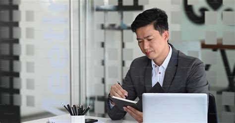 검은 양복을 입은 사업가가 노트북 컴퓨터로 작업하고 사무실 책상에 앉아 노트북에 메모를 하고 있다 사진 Unsplash의
