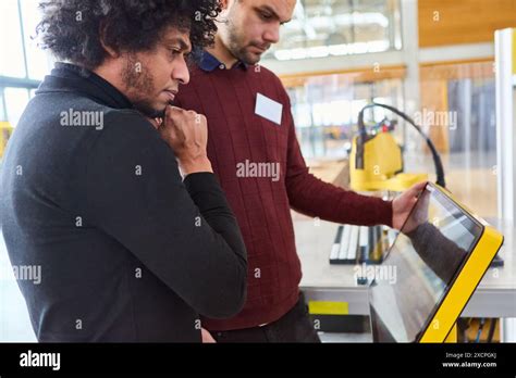 Two Engineers Focused On Programming A Robotic Arm In A Modern