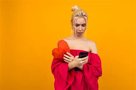 오렌지 스튜디오 배경에 종이에서 휴대 전화와 빨간 마음을 들고 빨간 드레스를 입은 슬픈 백인 금발 소녀 18 19세에 대한 스톡 사진 및 기타 이미지 Istock