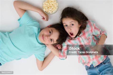 팝콘 그릇을 들고 카메라에 미소를 짓고 놀라움과 놀라움을 표현하고 하얀 스튜디오 배경에 등을 대고 누워 있는 행복한 아이들 2