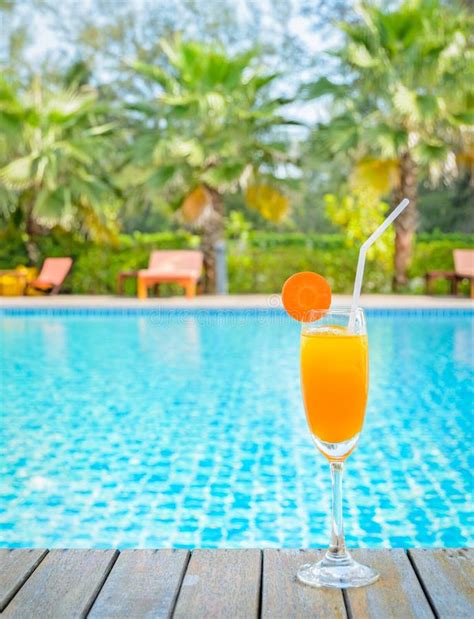 Orange Juice Glass On Wooden Table With Swimming Pool View Background