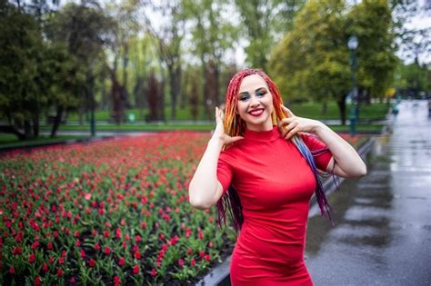 여러 가지 색상의 아프리카 머리띠와 꽉 빨간 드레스에 밝은 표현 메이크업을 가진 귀여운 소녀는 봄의 도착을 즐기는 공원에서 회전 땋은 머리에 대한 스톡 사진 및 기타 이미지