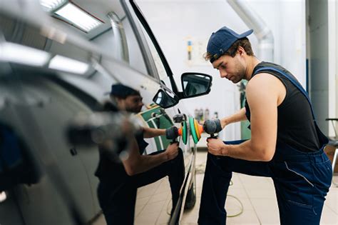 궤도 광택기와 함께 사용하는 자동차 수리점에서 고급 자동차의 문을 닦는 모자에 정비공 노동자의 근접 촬영 자동차 연마기를 사용하는 전문 자동차 페인트 기술자 25 29세에