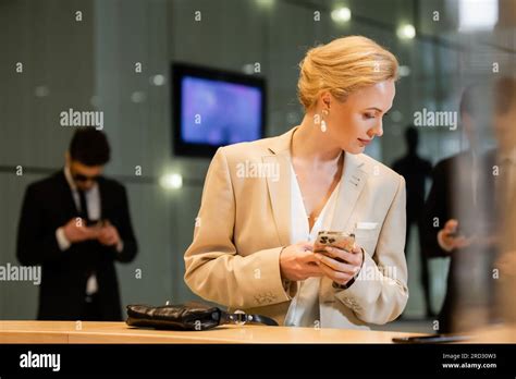 Personal Security Blonde Woman In Suit Holding Smartphone Near