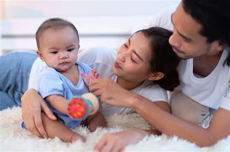 엄마와 아버지는 웃는 즐거운 자랑스러운 놀림 키스 뺨과 발 팔을 잡고 침대에서 새로 태어난 아시아 유아 아기를 잡고 가족에 대한 스톡 사진 및 기타 이미지 Istock