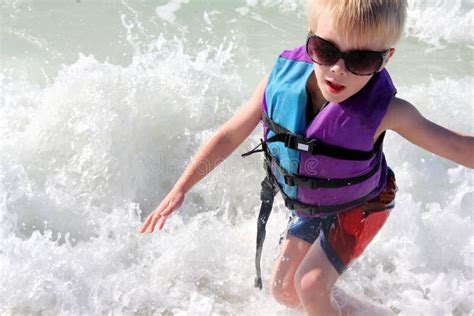 Niño Pequeño En El Chaleco Salvavidas Que Juega Con Agua En La Playa