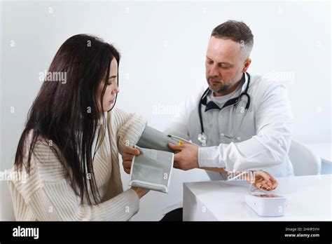 Male Doctor Puts On The Arm Of The Female Patient The Cuff Of Blood Pressure Monitor Stock Photo