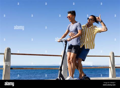 Happy Biracial Gay Male Couple Having Fun Riding Scooter Together On