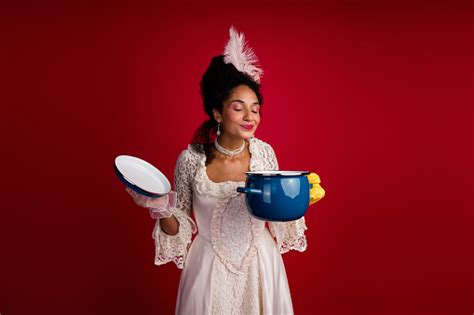 우아한 바로크 스타일의 드레스를 입은 젊은 여성이 생생한 붉은 배경에 파란색 냄비를 들고 과거와 현재의 융합을 보여줍니다 가사 집안일에 대한 스톡 사진 및 기타 이미지