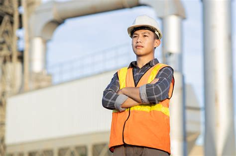 안전 조끼와 헬멧을 쓴 아시아 엔지니어 청년이 시멘트 공장에 서서 팀과 함께 작업을 성공으로 이끌었다 엔지니어링 시멘트 공장 노동자 개념 공장 산업 건물에 대한 스톡 사진