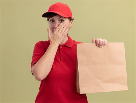 Free Photo Middle Aged Delivery Woman In Red Uniform And Cap Giving Paper Package Looking At