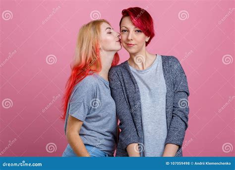 Two Lesbian Girls One Kisses Another On The Cheek On A Pink