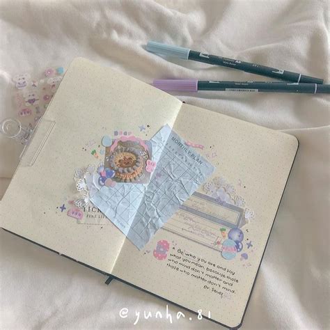 An Open Notebook Sitting On Top Of A Bed Next To Two Markers And A Pen