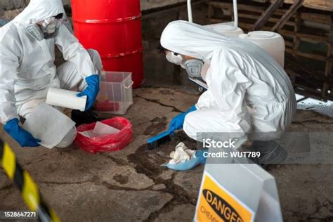 Ppe 슈트와 방독면을 착용한 두 명의 화학자로 구성된 팀이 공장 창고 바닥에서 치명적인 화학 물질 유출을 회수합니다 산업
