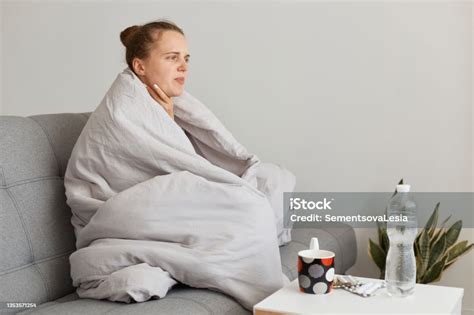 담요에 싸여 소파에 앉아 헤어 롤빵과 아픈 아픈 여자의 실내 샷은 나쁜 느낌 인플루엔자 증상을 갖는 인후통과 높은 온도를 앓고