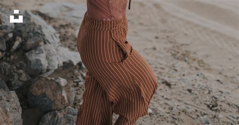 낮 동안 갈색 모래 위에 서 있는 검은 모자를 쓰고 갈색과 검은색 줄무늬 드레스를 입은 여자 사진 Unsplash의 무료 회색 이미지