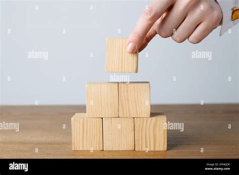 Woman Building Pyramid Of Cubes On Wooden Table Against Light Background Closeup Space For