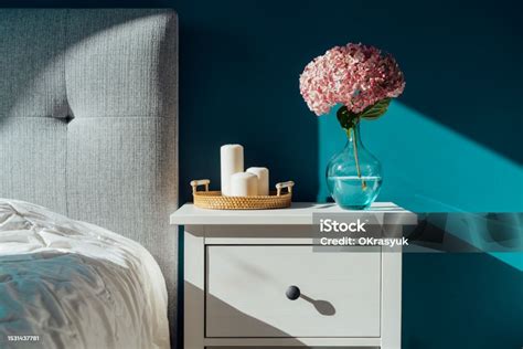 어두운 색상의 세련되고 현대적인 아늑한 침실 청록색 벽 가정 장식으로 아늑한 인테리어 회색 패브릭 헤드보드 흰색 담요 침대 옆 탁자 분홍색 수국 꽃병 양초가 있는 침대 고급