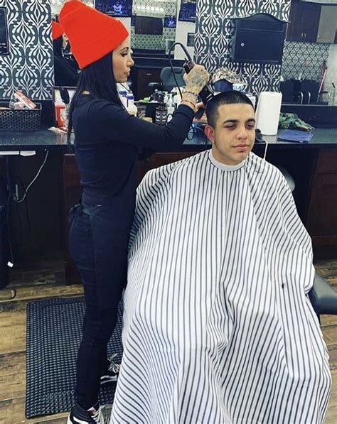 A Man Getting His Hair Cut By A Woman In A Barbershop With A Red Beanie
