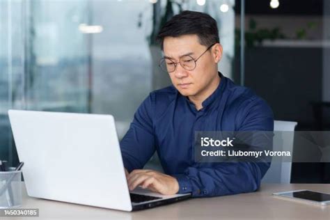 현대 사무실에서 일하는 진지한 생각의 아시아 사업가 직장에서 노트북을 사용하는 셔츠와 안경을 쓴 성숙한 남자 복잡한 결정을
