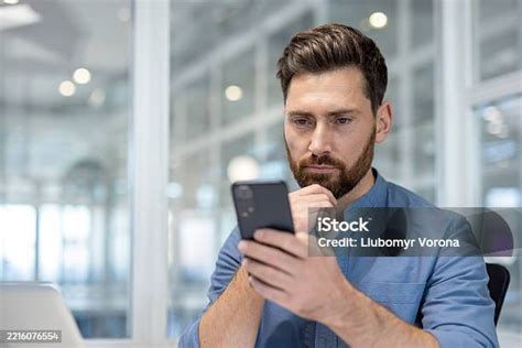 진지한 남자가 손에 전화기를 들고 앉아 있고 사업가가 생각하고 온라인 이메일을 읽고 있습니다 사무실 내 직장에서 회사 직원 클로즈업 35 39세에 대한 스톡 사진 및 기타
