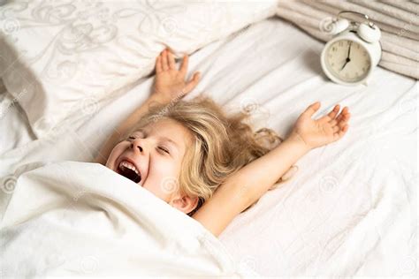 Счастливая блондинка в белой кровати с будильником доброе утро Стоковое Изображение