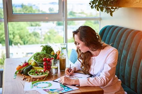 배경에 녹색 사무실에서 다른 건강 식품 재료와 함께 앉아 다이어트 계획에 작업 하는 테이프 측정 의료 제복을 입은 여성 영양사 체중 감량과 올바른 영양 개념 개념에 대한