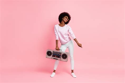 핑크색 배경에 고립 된 재미를 가진 테이프 플레이어를 들고 다니는 꽤 시원하고 기쁜 쾌활한 쾌활한 물결 모양의 머리 소녀의 전체 길이 몸 크기보기 갈색 머리에 대한 스톡