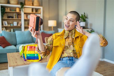 집에서 짧은 머리를 하고 손에 카메라를 들고 Lgbt 커뮤니티의 간판을 들고 얼굴에 미소를 띠고 다리를 테이블 위에 올려놓은 채