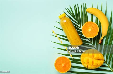 신선한 오렌지 바나나 파인애플 망고 스무디와 손바닥에 수 분이 많은 과일 파란색 배경 위에 나뭇잎 여름 음료를 해독 채식