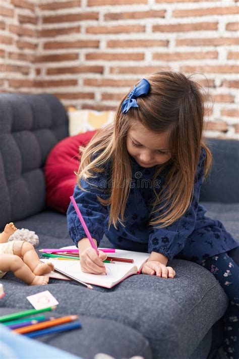 Adorable Hispanic Girl Drawing On Notebook Sitting On Sofa At Home