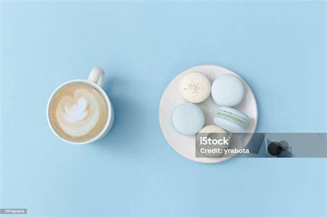 밝은 파란색 배경에 맛있는 마카롱과 큰 찻잔과 흰색 접시에 Coffe 카푸치노 아트 폼 달콤한 음식 개념입니다 맨 위 보기 플랫