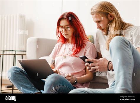 White Man And Woman Using Cellphone And Laptop While Sitting On Floor
