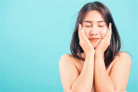 웃는 얼굴 아시아의 아름다운 여성은 텍스트 복사 공간이 있는 파란색 배경에 감동적인 얼굴 피부 관리를 제공합니다 프리미엄 사진