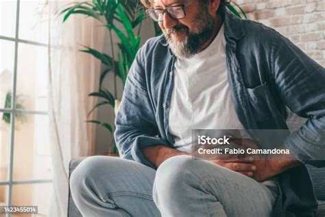 집에 앉아있는 심한 복통으로 고통받는 남자 통증 설사 또는 소화 불량 문제로 고통받는 복부를 들고있는 성숙한 남자의 손 고통스러운 감각으로 배를 누르는 백인 남자 남자에