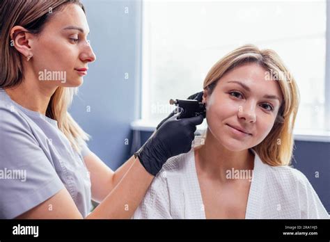 Close Up Of Face Of Young Blonde Woman Doing Ear Piercing Procedure Doctor Hands In Black