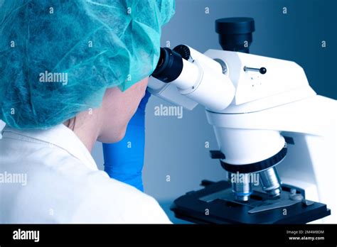 Female Scientist Looking Under A Light Microscope In A Science Lab Blue Atmosphere That Evokes